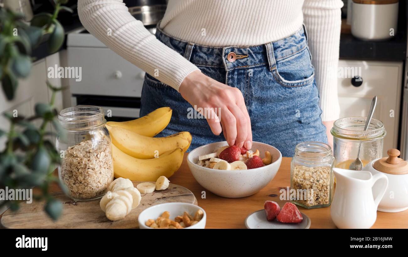 Adding fruits to breakfast oatmeal porridge bowl. Woman preparing ...