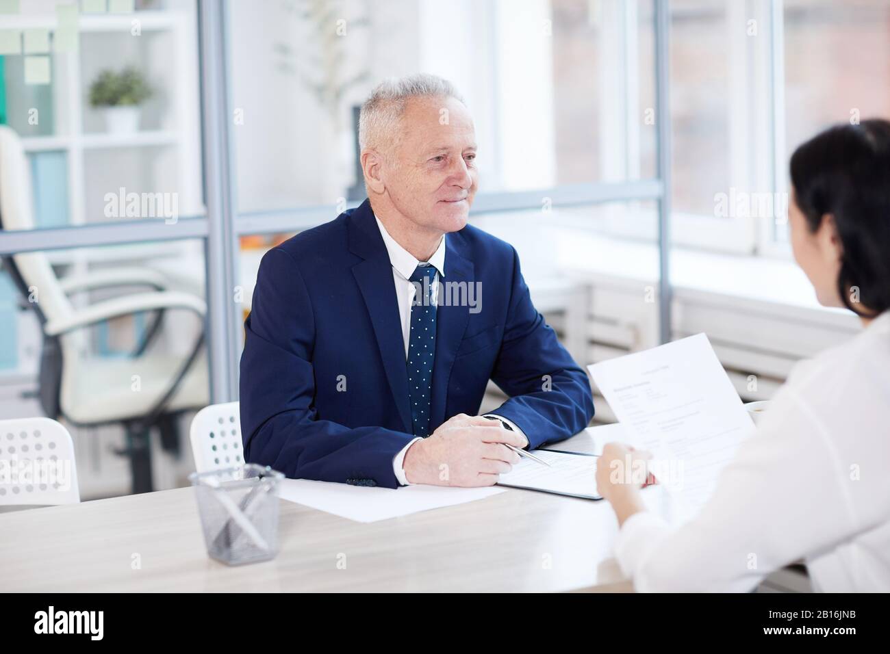 Portrait of smiling senior businessman interviewing young woman for job ...