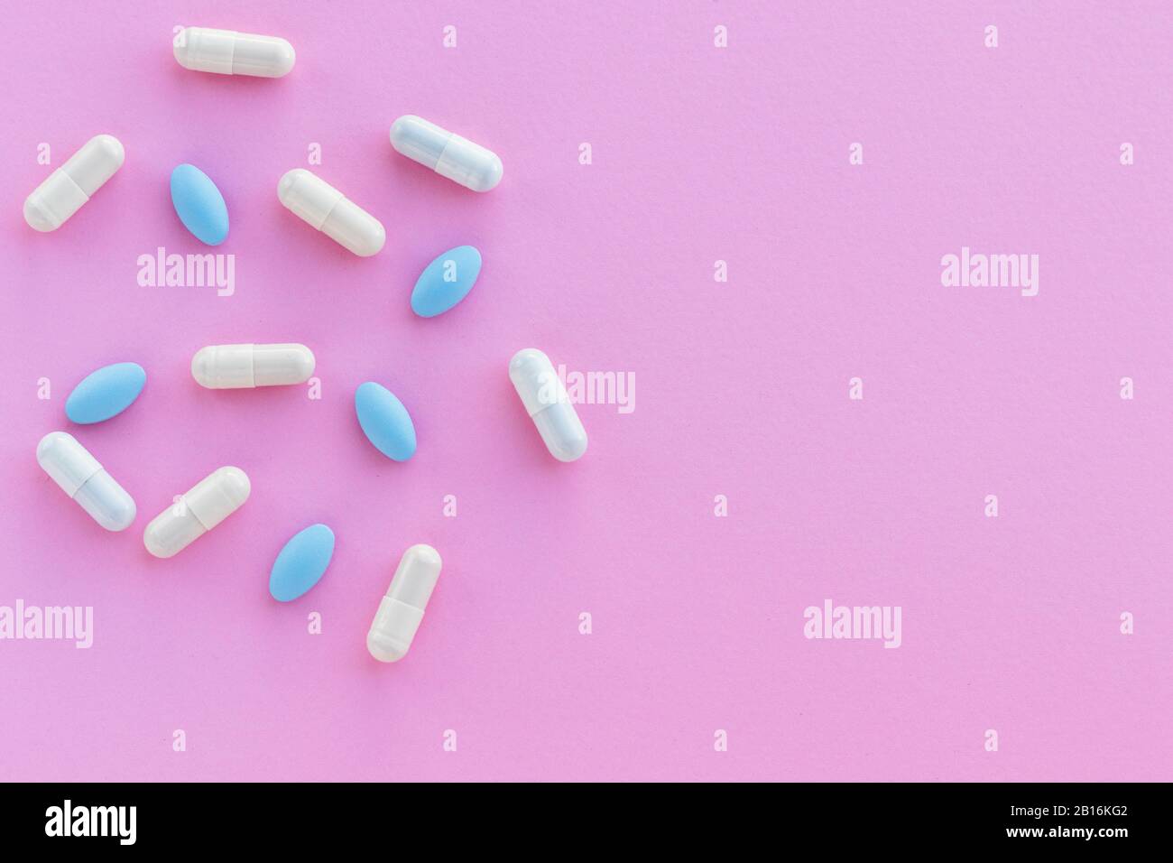 Blue pills and white capsules isolated on light pink background. Woman ...