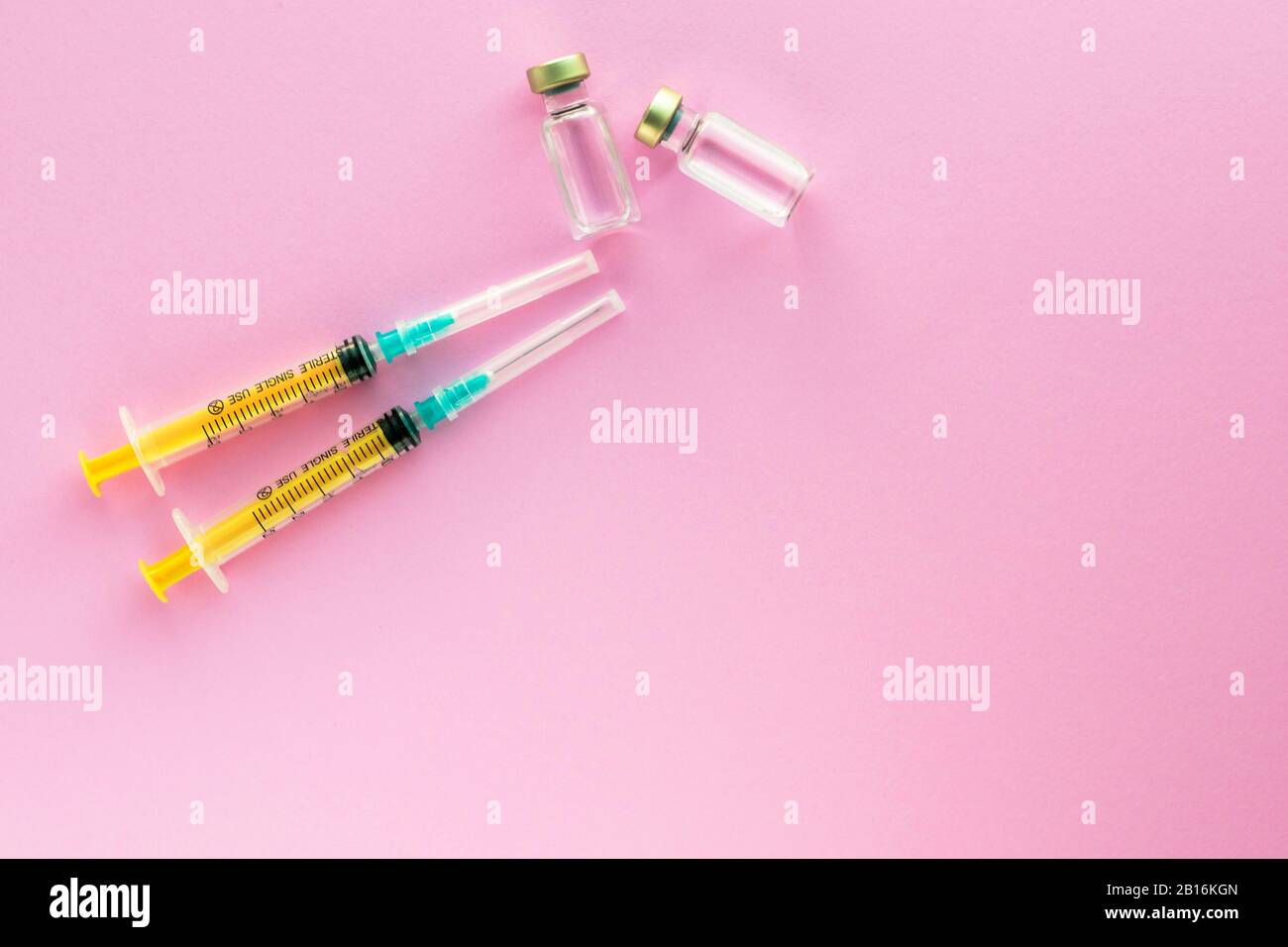 Two syringes and glass vials with liquid on light pink background ...