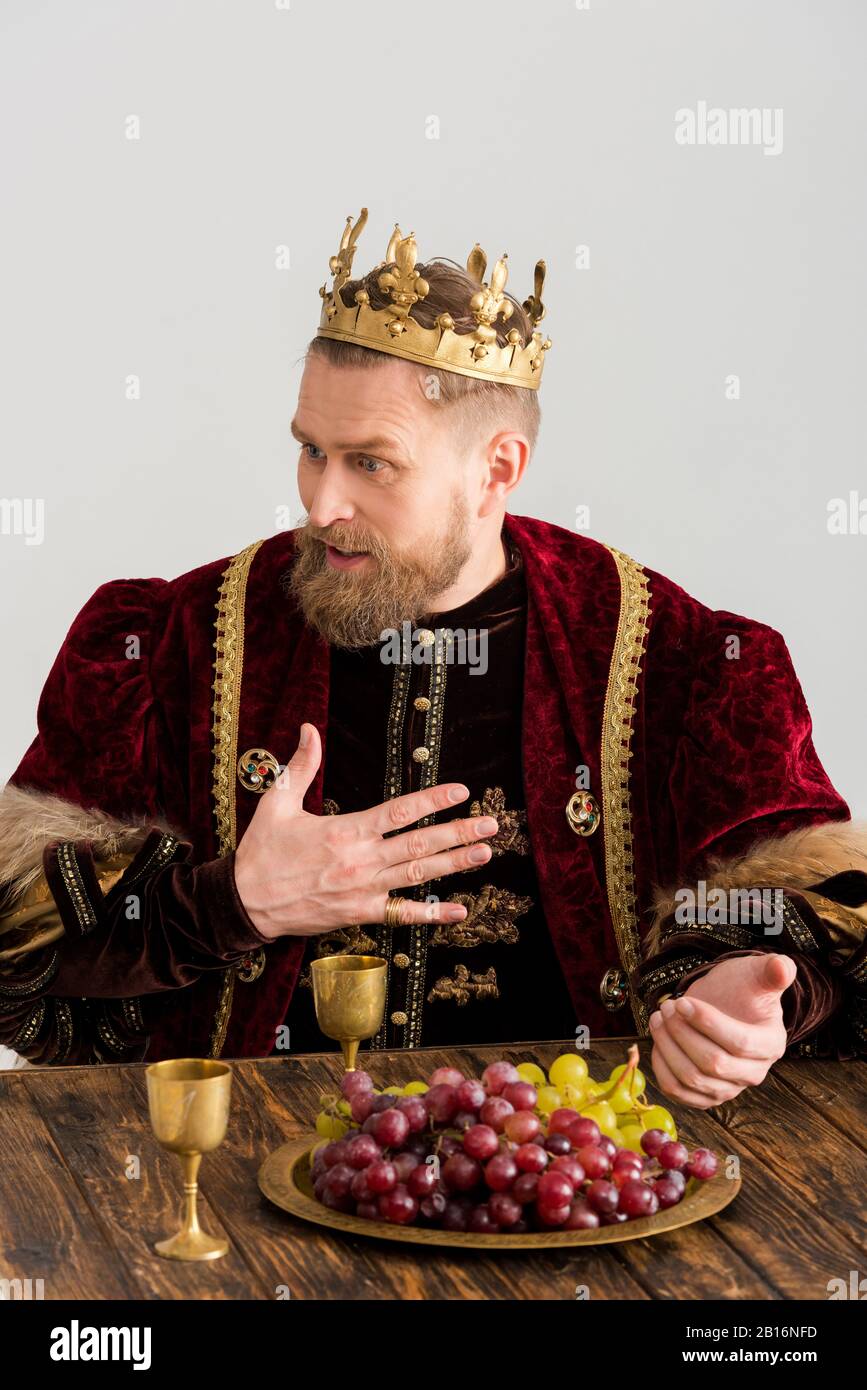 shocked man with crown sitting at table isolated on grey Stock Photo ...