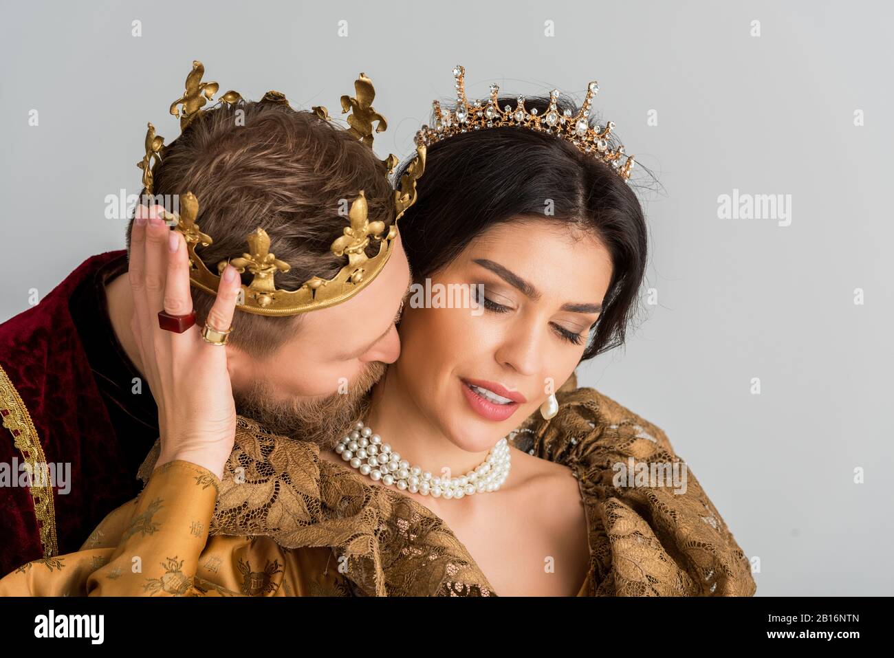 king with crown hugging and kissing attractive queen isolated on grey ...