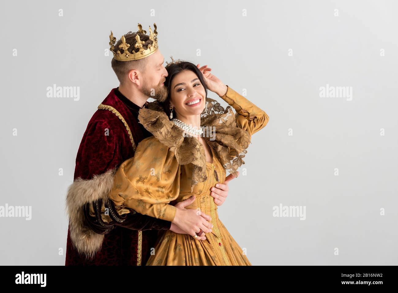 king with crown kissing and hugging smiling queen isolated on grey ...