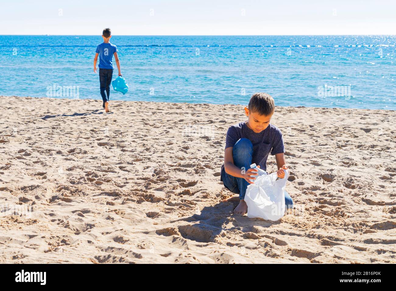 Volunteers cleaning beach from plastic. Boys walking on the beach and ...