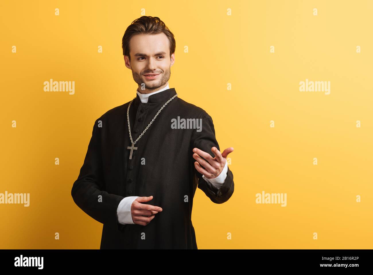 smiling catholic priest standing with outstretched hand while looking ...