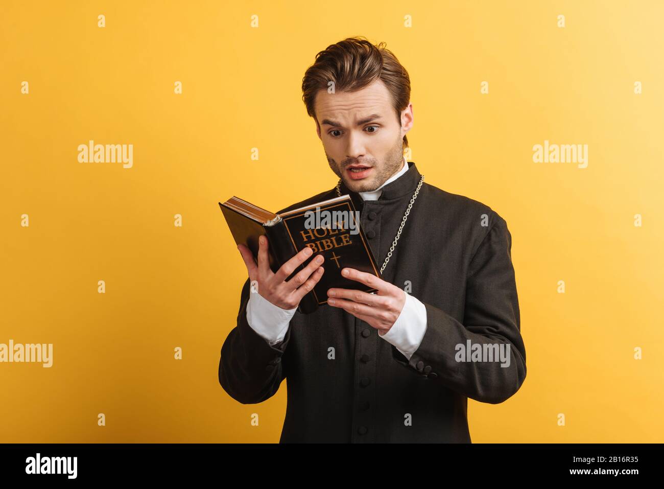 shocked catholic priest reading holy bible isolated on yellow Stock ...
