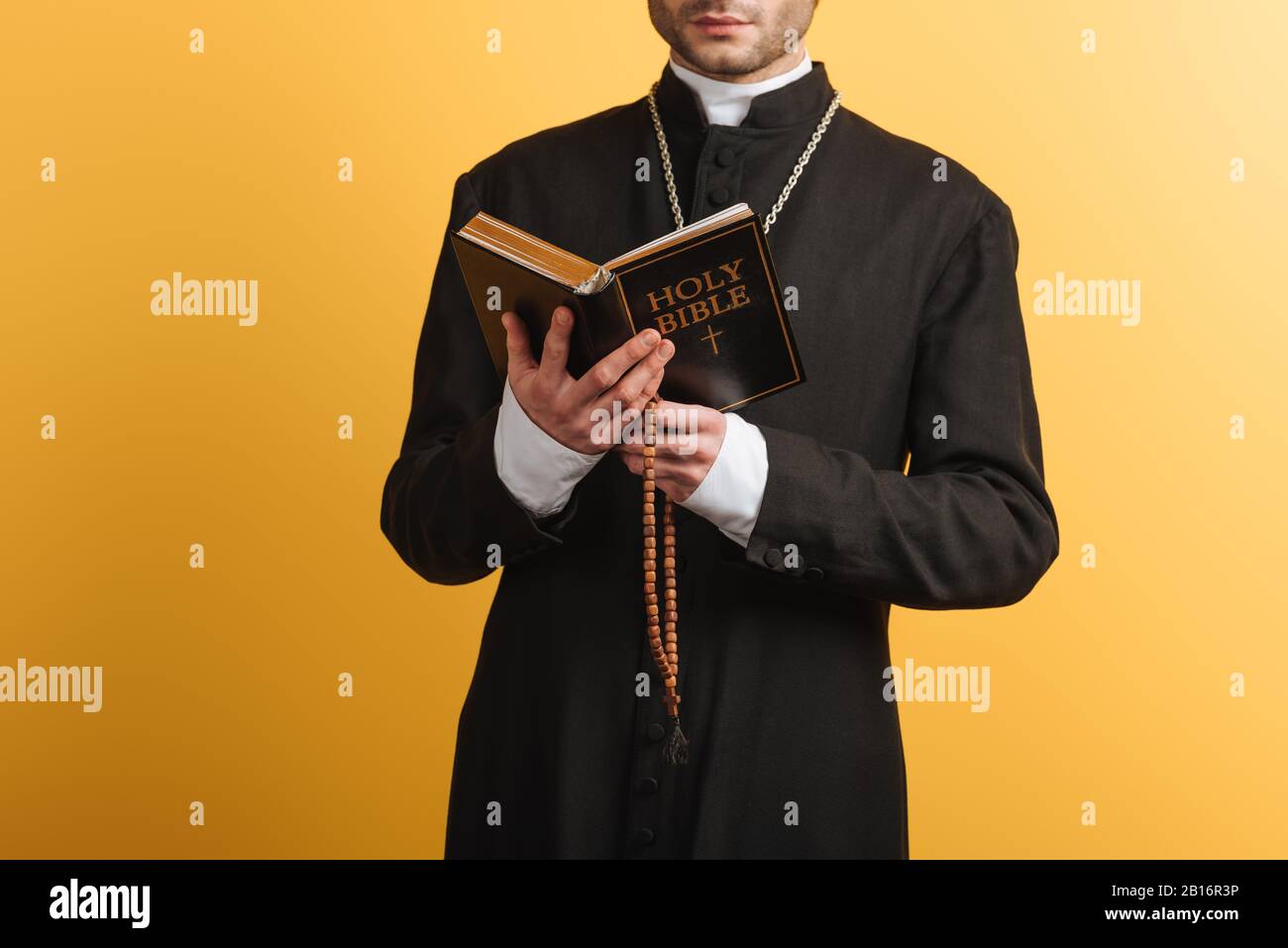 cropped view of catholic priest reading bible and holding wooden rosary ...