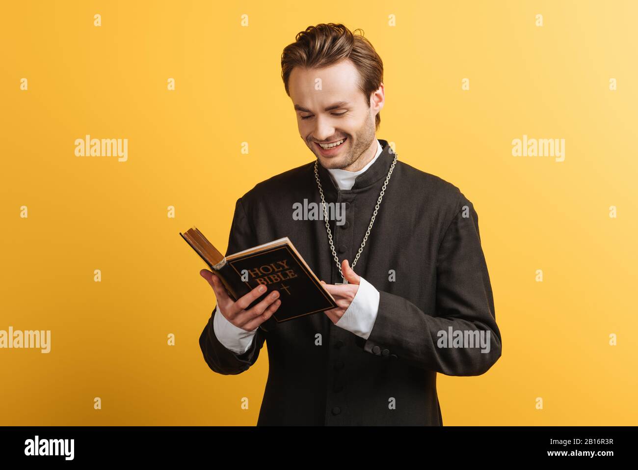 cheerful catholic priest laughing while reading bible isolated on ...
