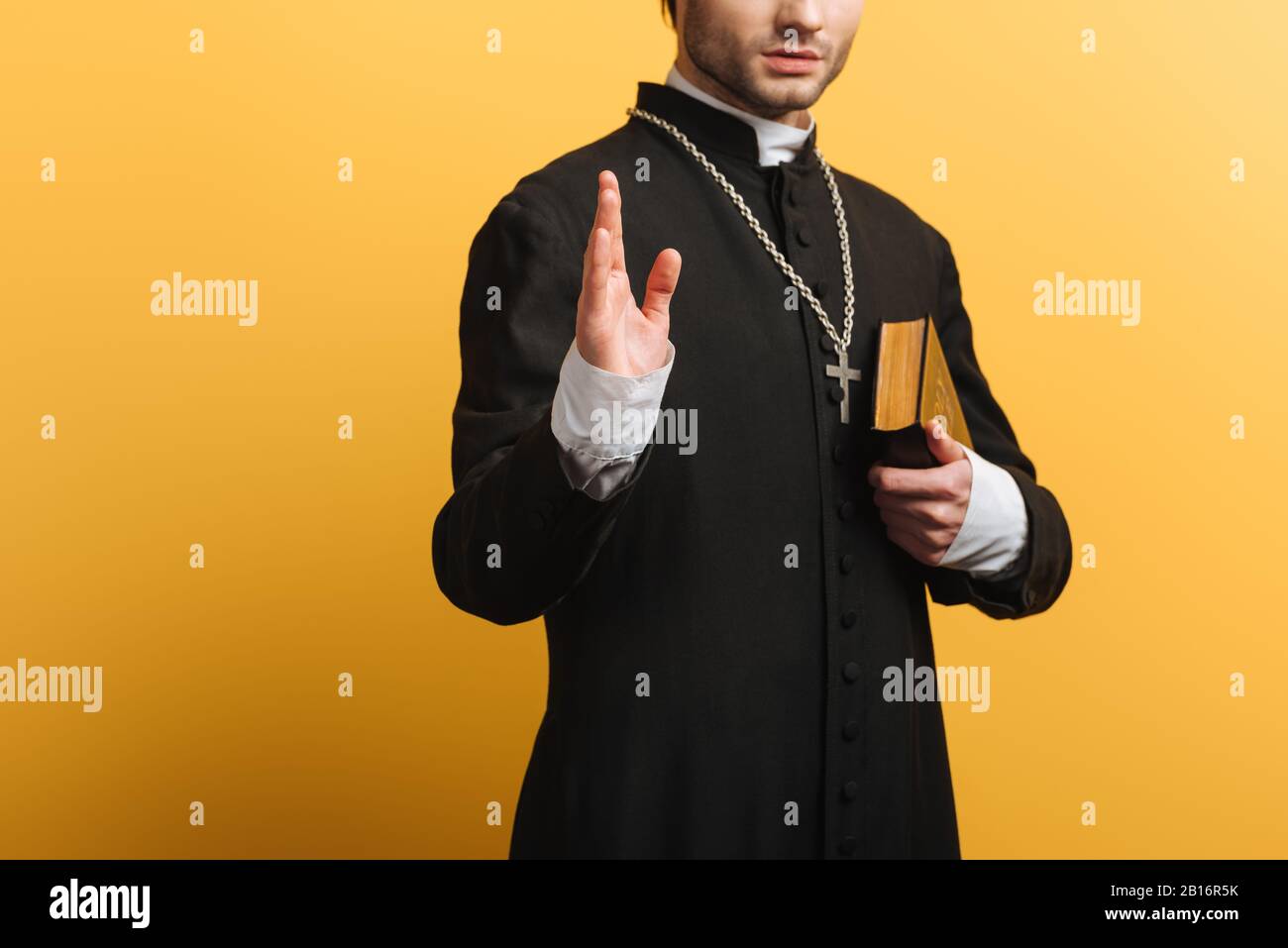 cropped view of catholic priest showing blessing gesture while holding ...