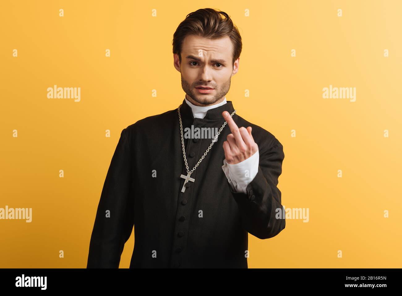 displeased catholic priest showing middle finger isolated on yellow ...