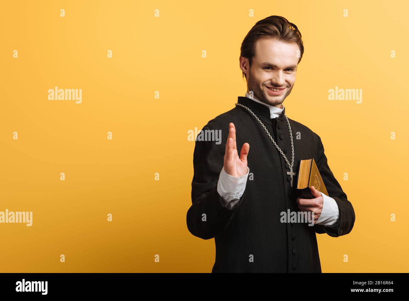 smiling catholic priest showing blessing gesture while holding bible ...