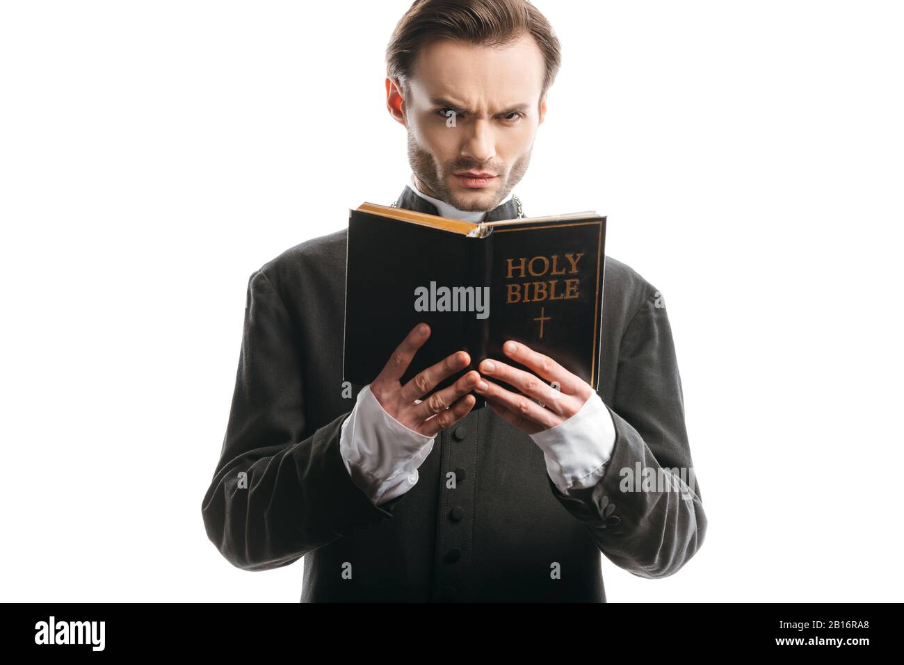 frowning catholic priest looking at camera while holding holy bible ...