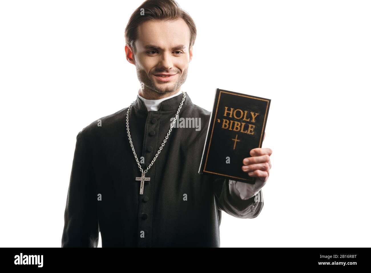 young catholic priest smiling while holding holy bible isolated on ...