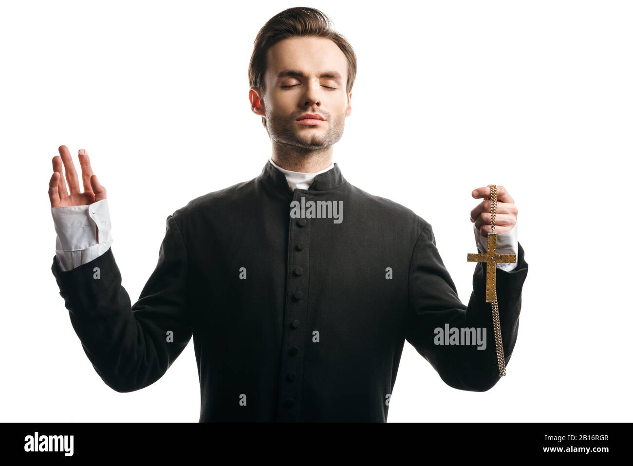 concentrated catholic priest praying with raised hand while holding ...