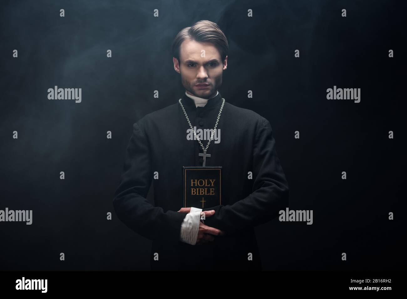 young confident catholic priest looking at camera while holding holy ...