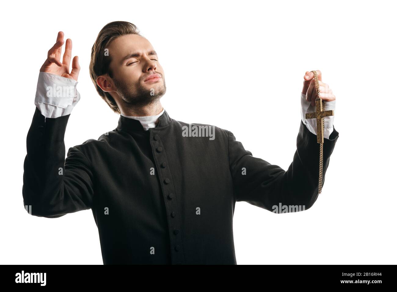 young catholic priest praying with closed eyes and raised hands while ...