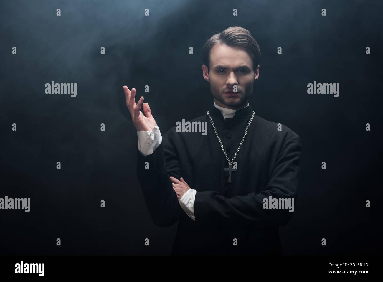 young confident catholic priest standing with open arm on black ...