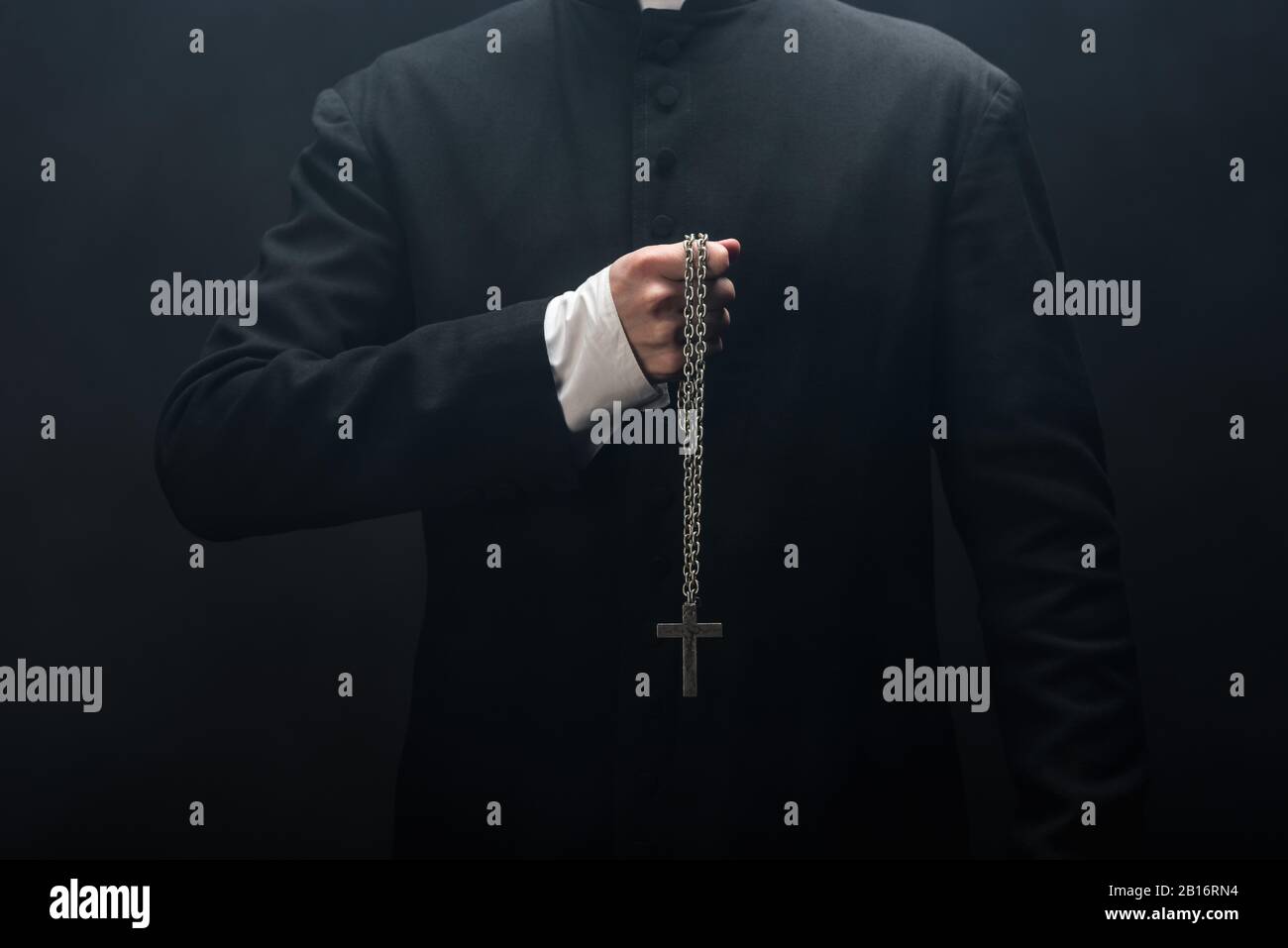 cropped view of catholic priest holding necklace with silver cross ...