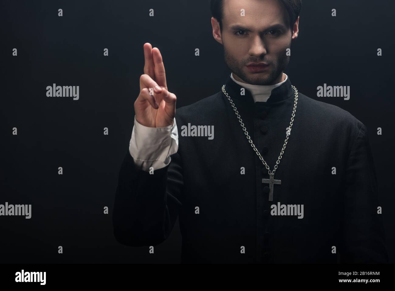 young confident catholic priest looking at camera and showing blessing ...