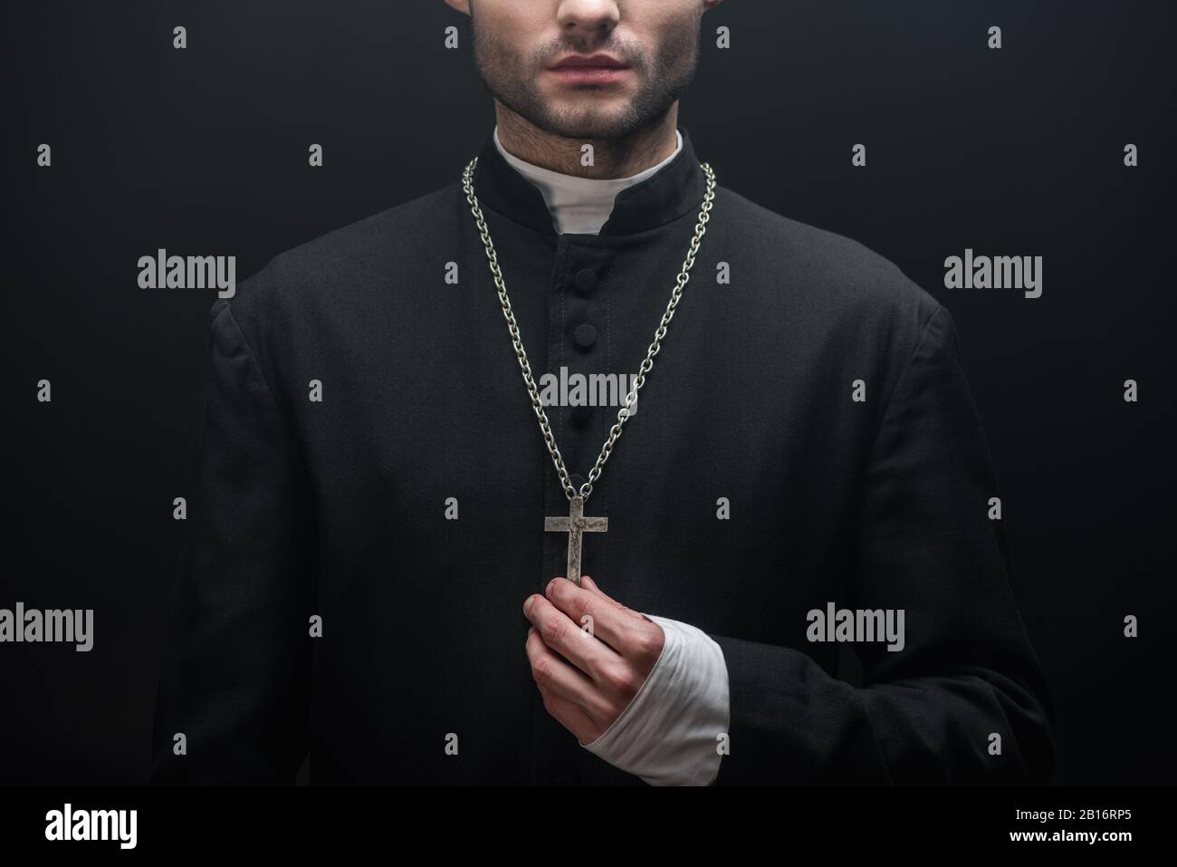 cropped view of catholic priest touching silver cross isolated on black ...
