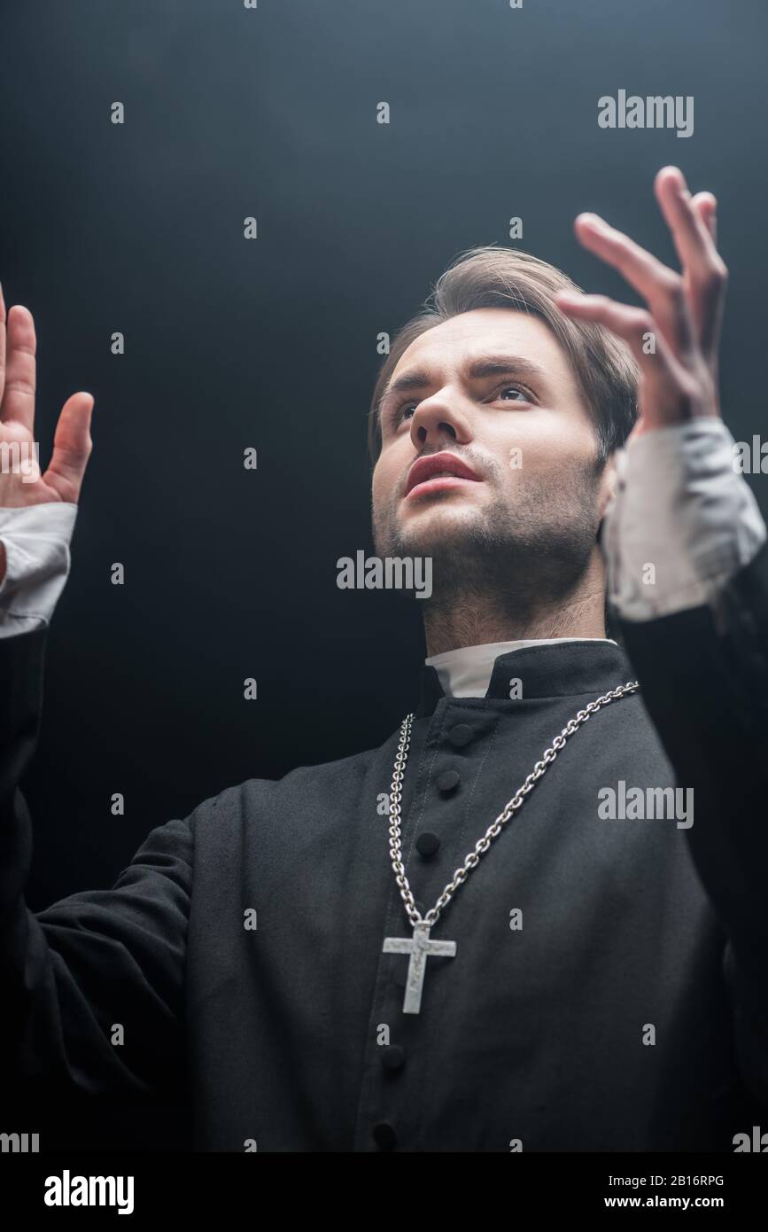 Low Angle View Of Young Serious Catholic Priest Praying With Raised