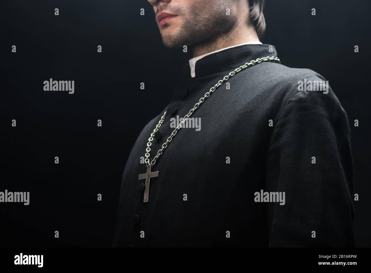 cropped view of catholic priest in black cassock with silver cross on ...