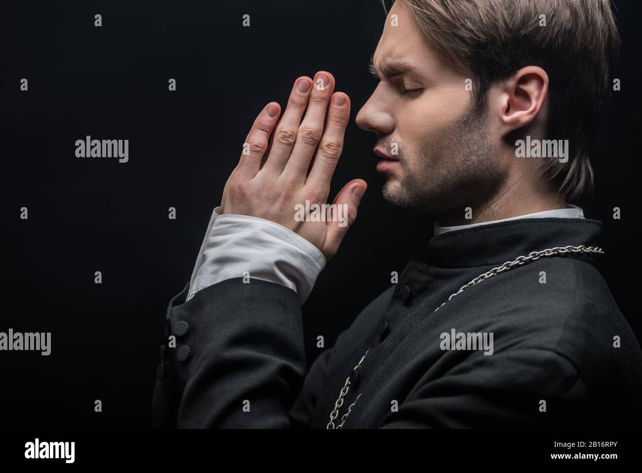 side view of young concentrated catholic priest praying with closed ...