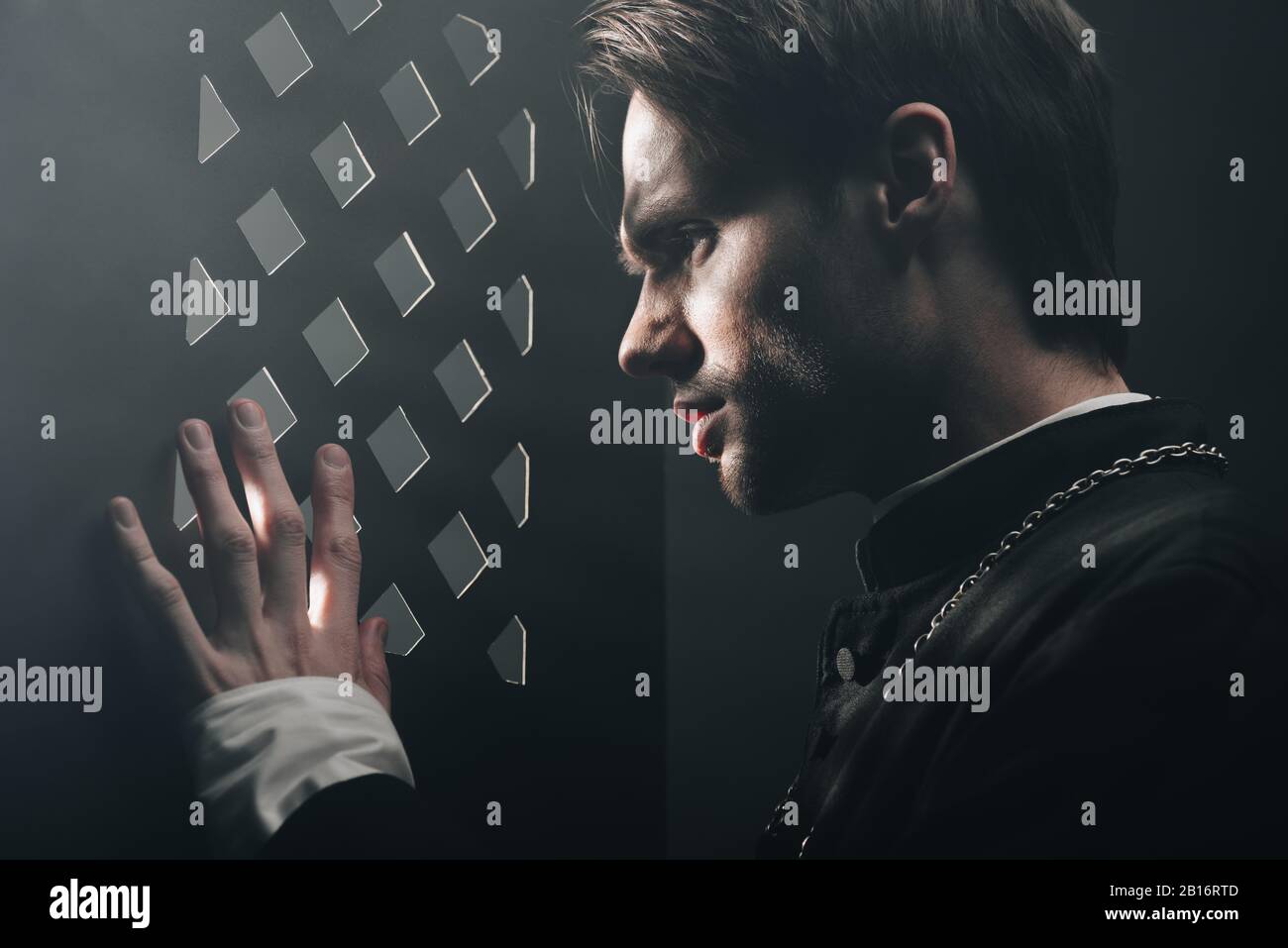 young tense catholic priest looking through confessional grille in dark ...