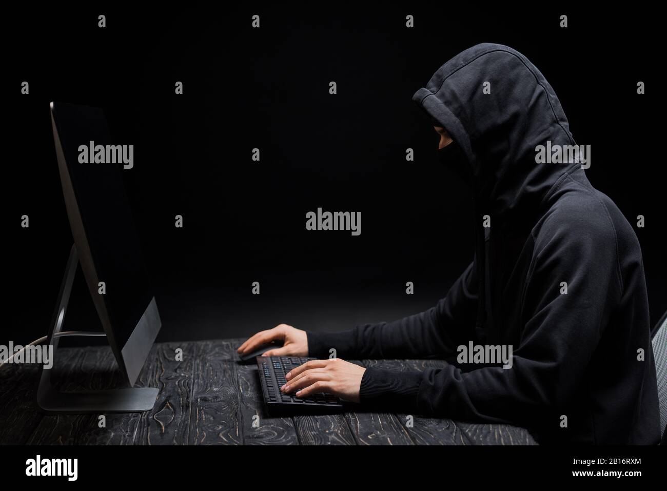 hacker in hood looking at computer monitor with blank screen on black ...