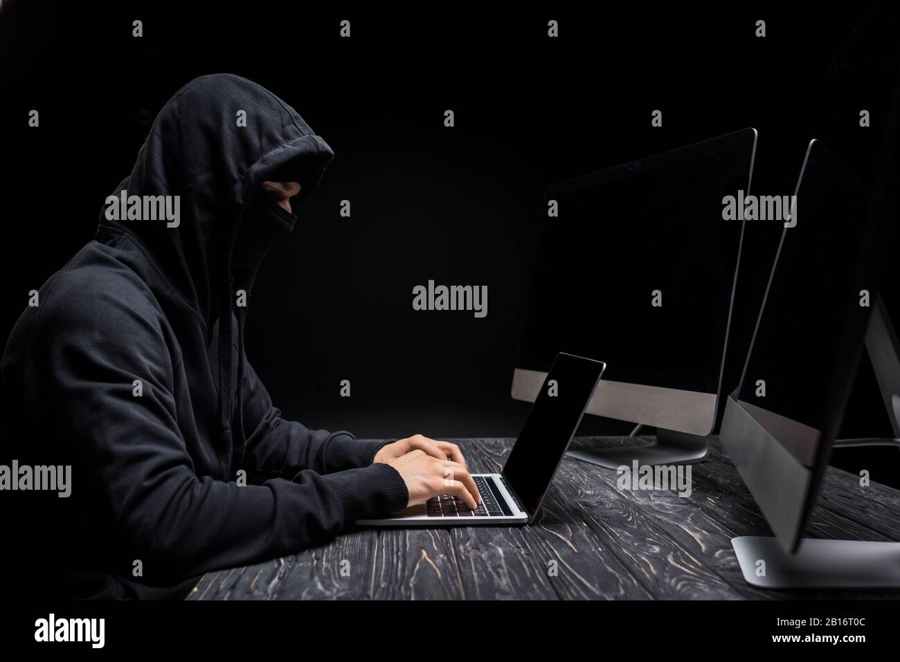 back view of hooded hacker with hands behind head near computer ...