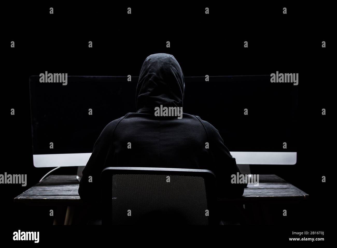 back view of hacker sitting near computer monitors with blank screen ...