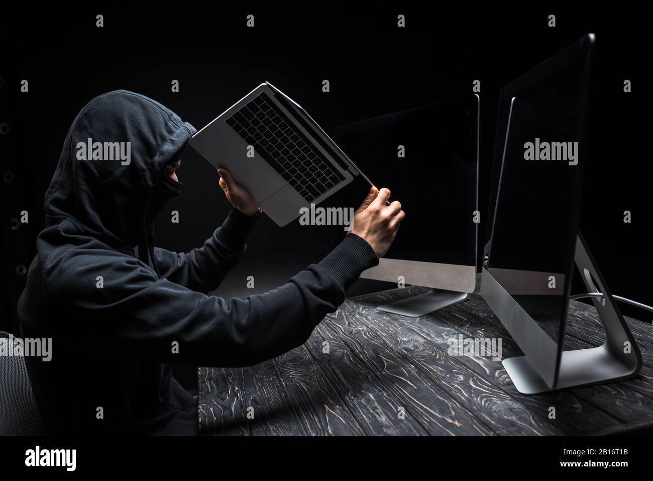 hacker holding laptop near computer monitors with blank screen isolated ...