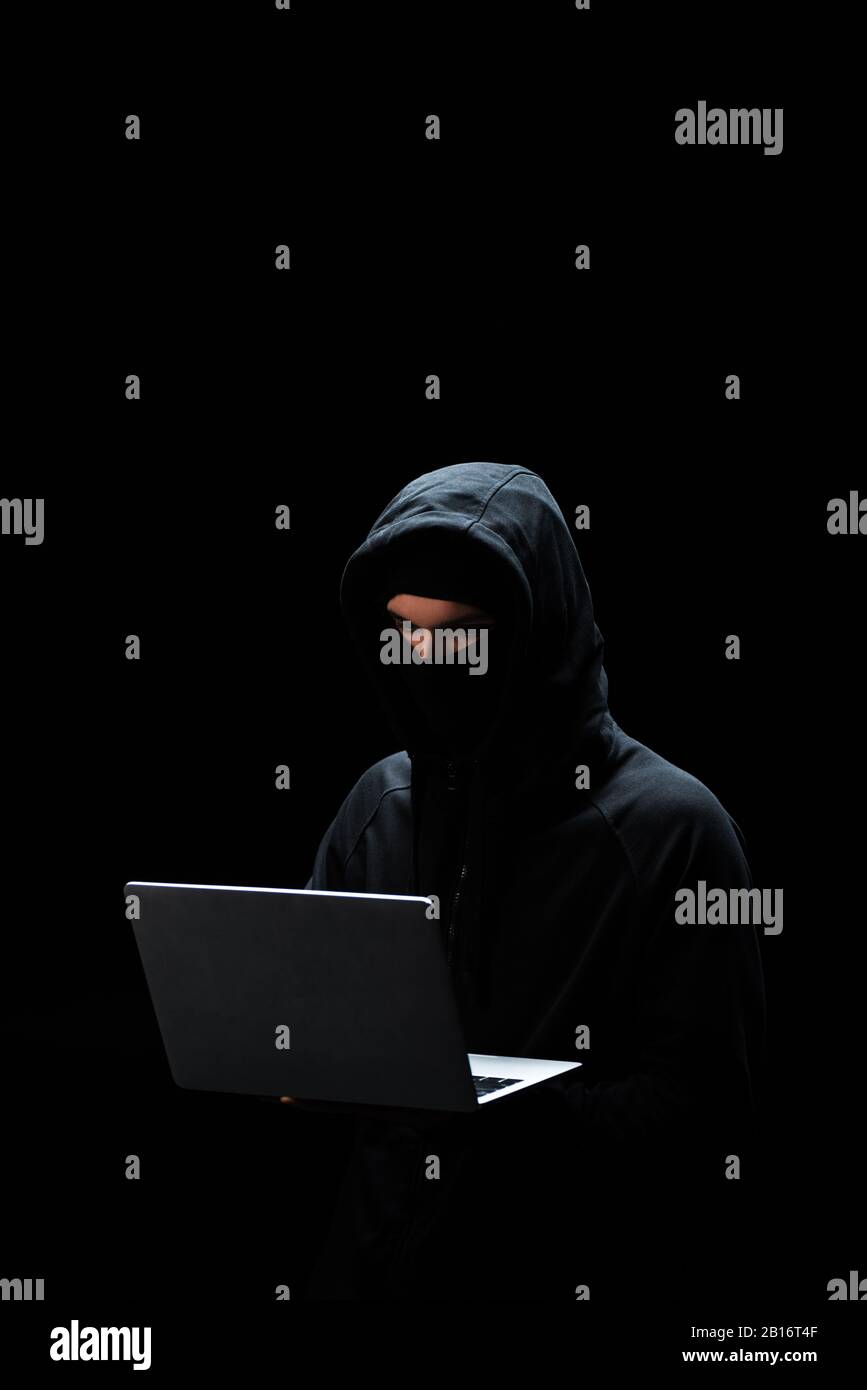 young hacker in hood using laptop isolated on black Stock Photo - Alamy