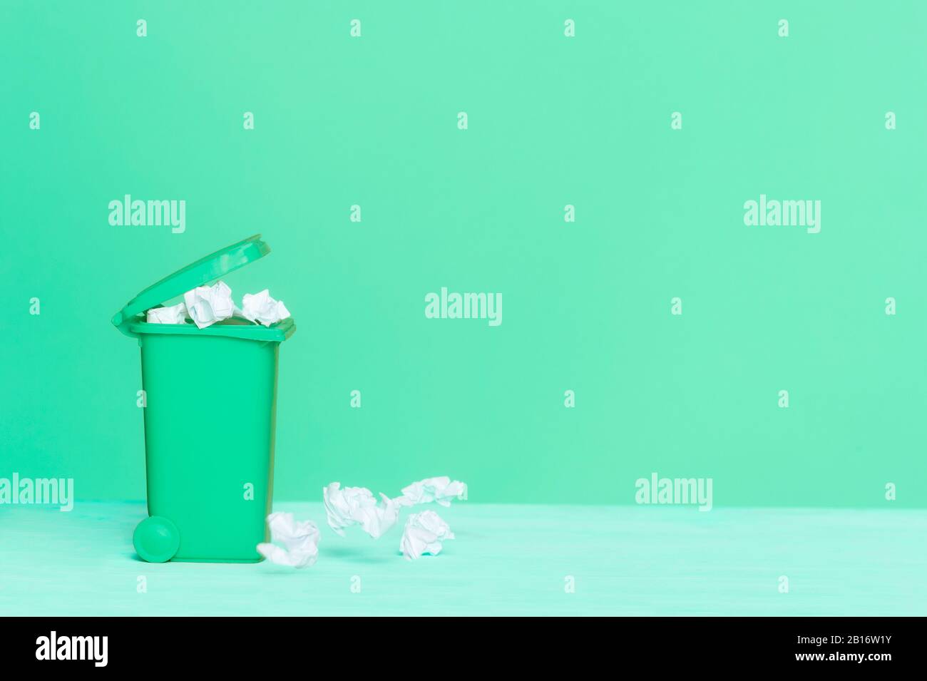 A green plastic garbage bin and paper on green background, great for ...