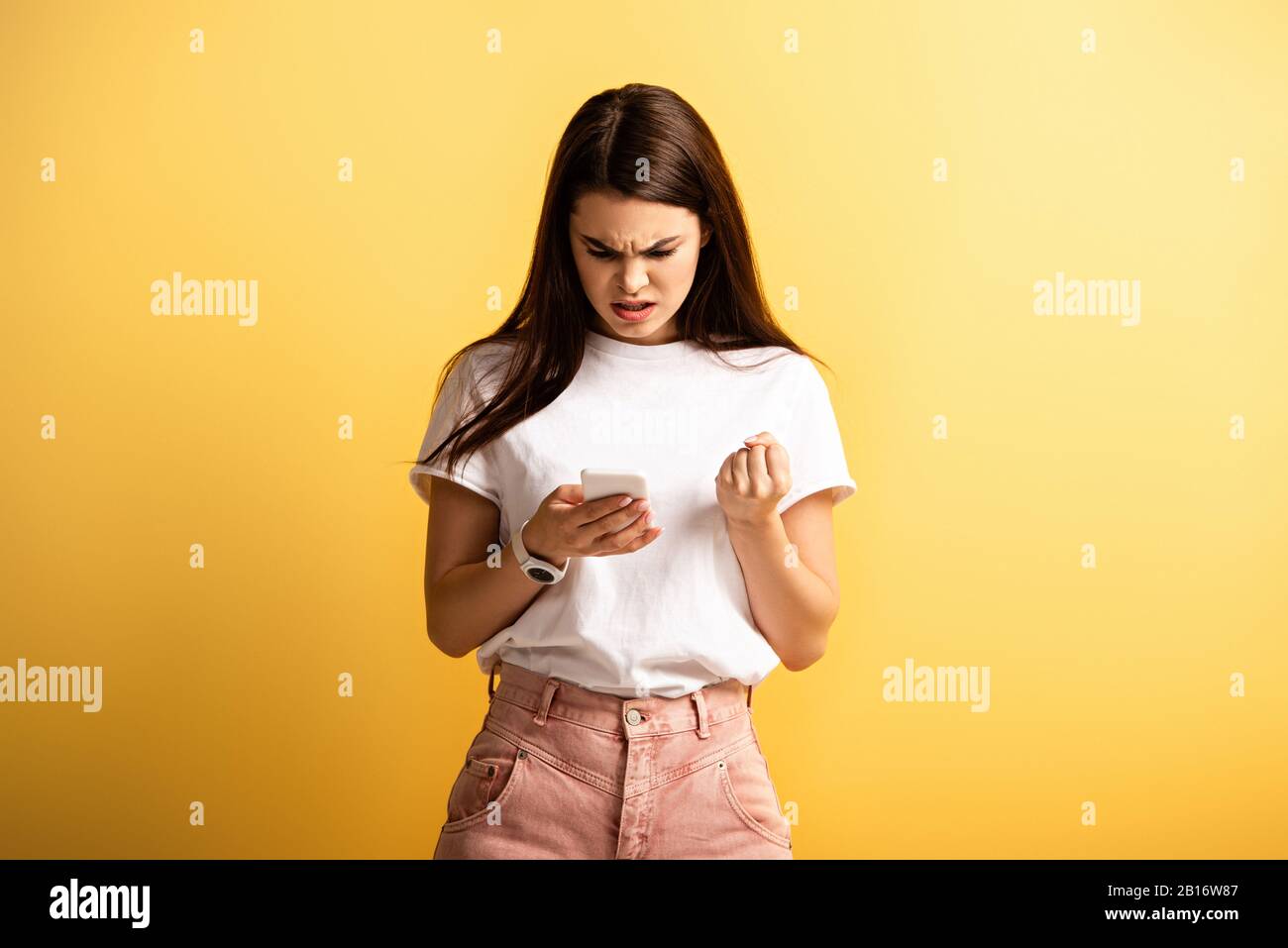 angry girl holding clenched fist while talking on smartphone on yellow ...