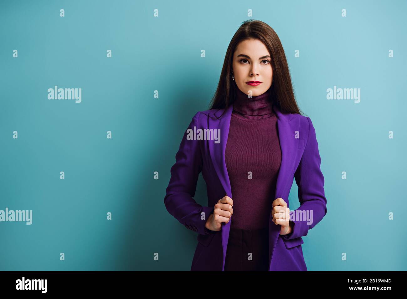 attractive, confident girl looking at camera while standing on blue ...