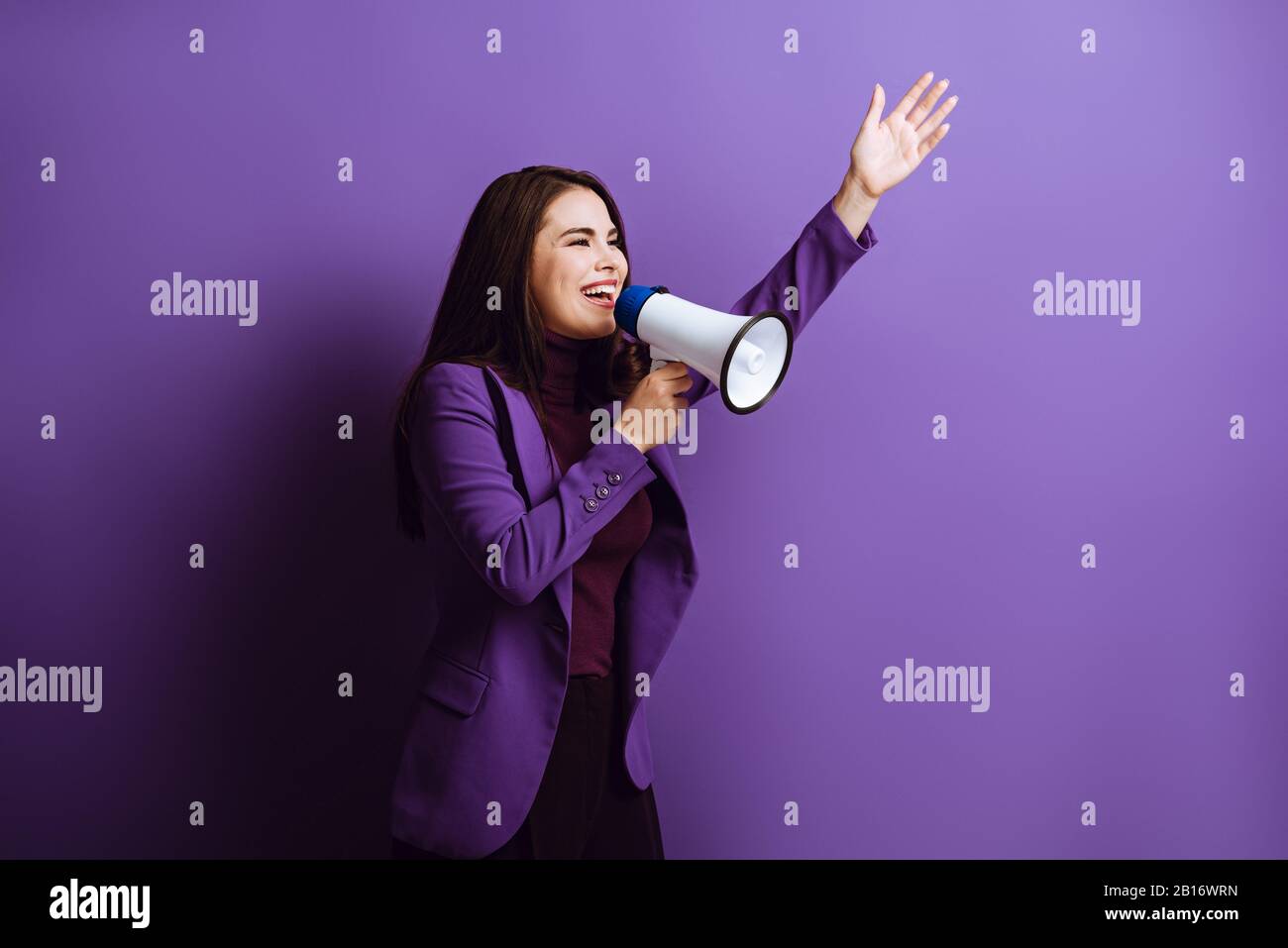 excited young woman talking in megaphone while standing with raised ...