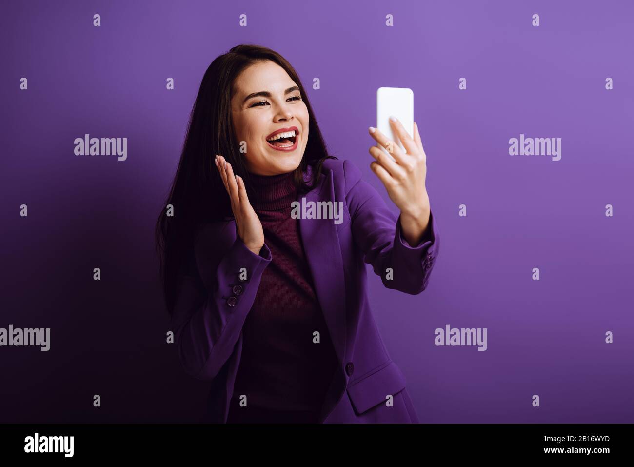 happy girl waving hand while having video call on purple background ...