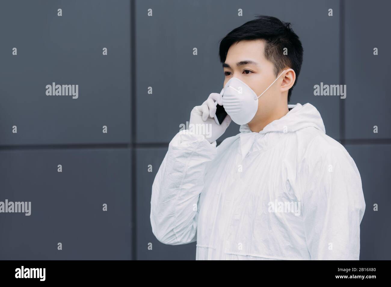 asian epidemiologist in hazmat suit and respirator mask talking on ...