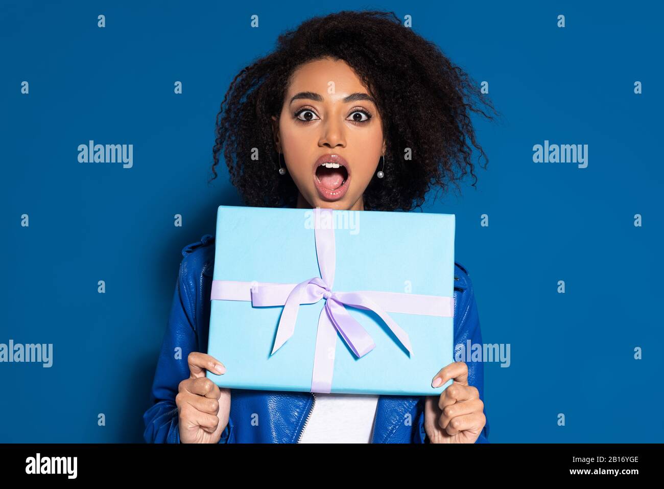 shocked african american woman holding present on blue background Stock ...