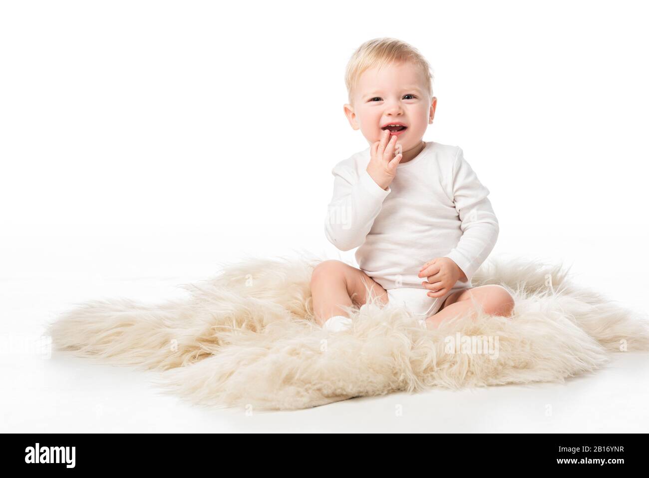 Cute child touching chin with open mouth, sitting on fur on white ...
