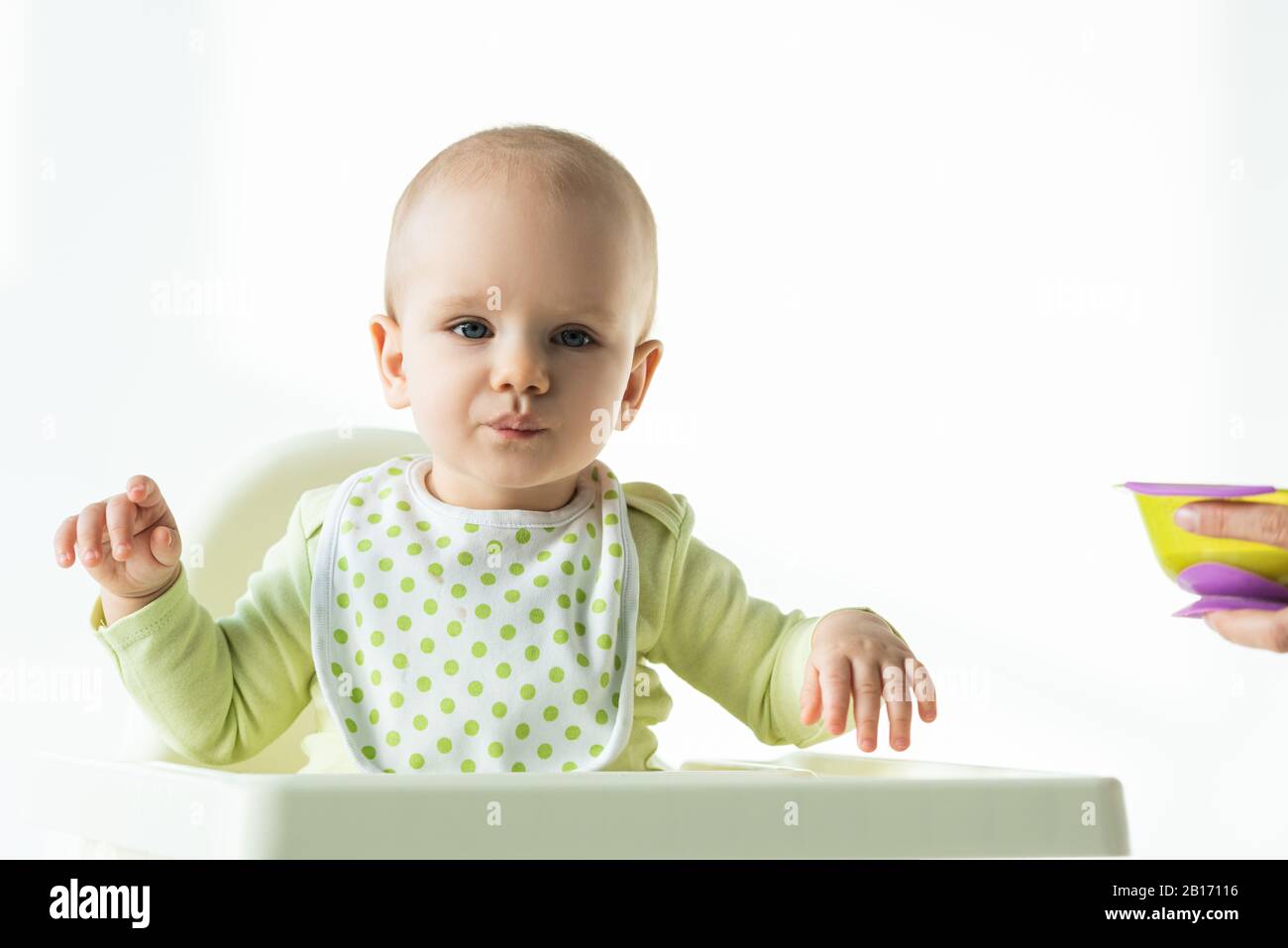Adorable baby looking at camera while sitting on feeding chair near ...