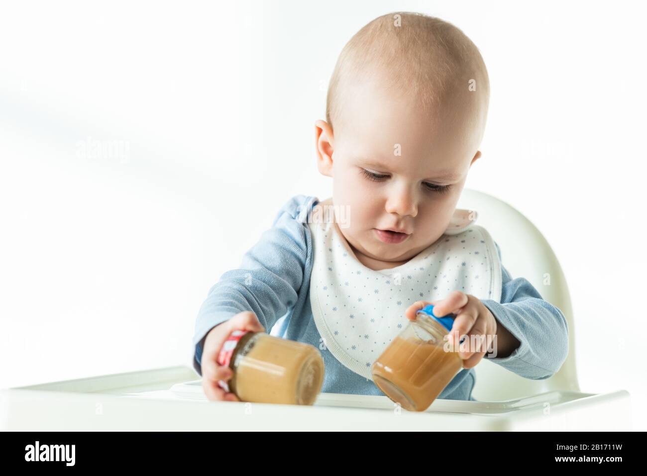 Baby holding jars of fruit puree while sitting on feeding chair on ...