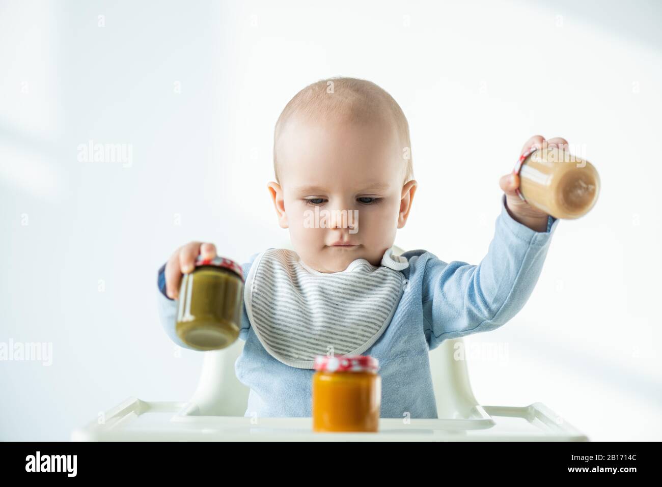 Selective focus of baby holding jars of vegetable baby nutrition while ...