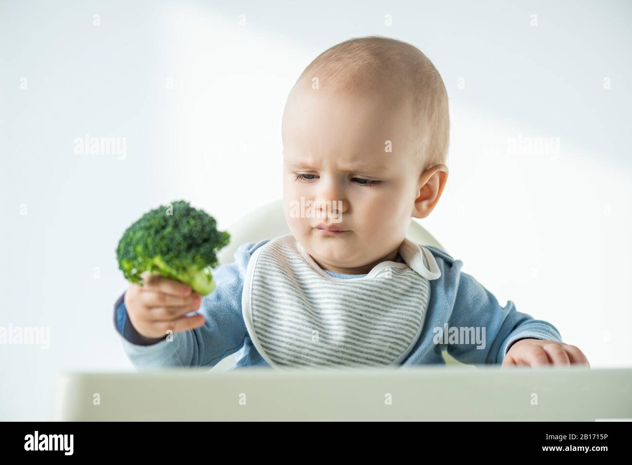 Selective focus of baby holding piece of broccoli while sitting on ...