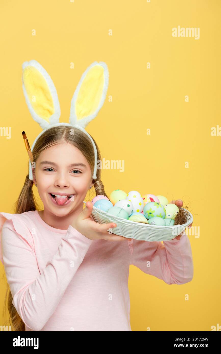 cheerful kid with bunny ears sticking out tongue and holding easter ...