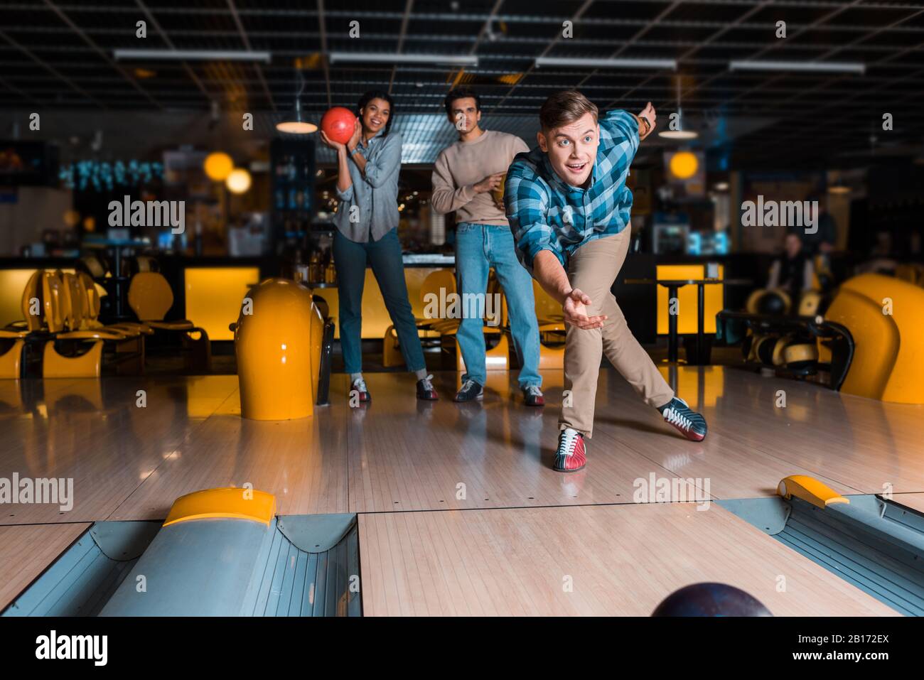 smiling young man throwing bowling bowl on skittle alley near ...