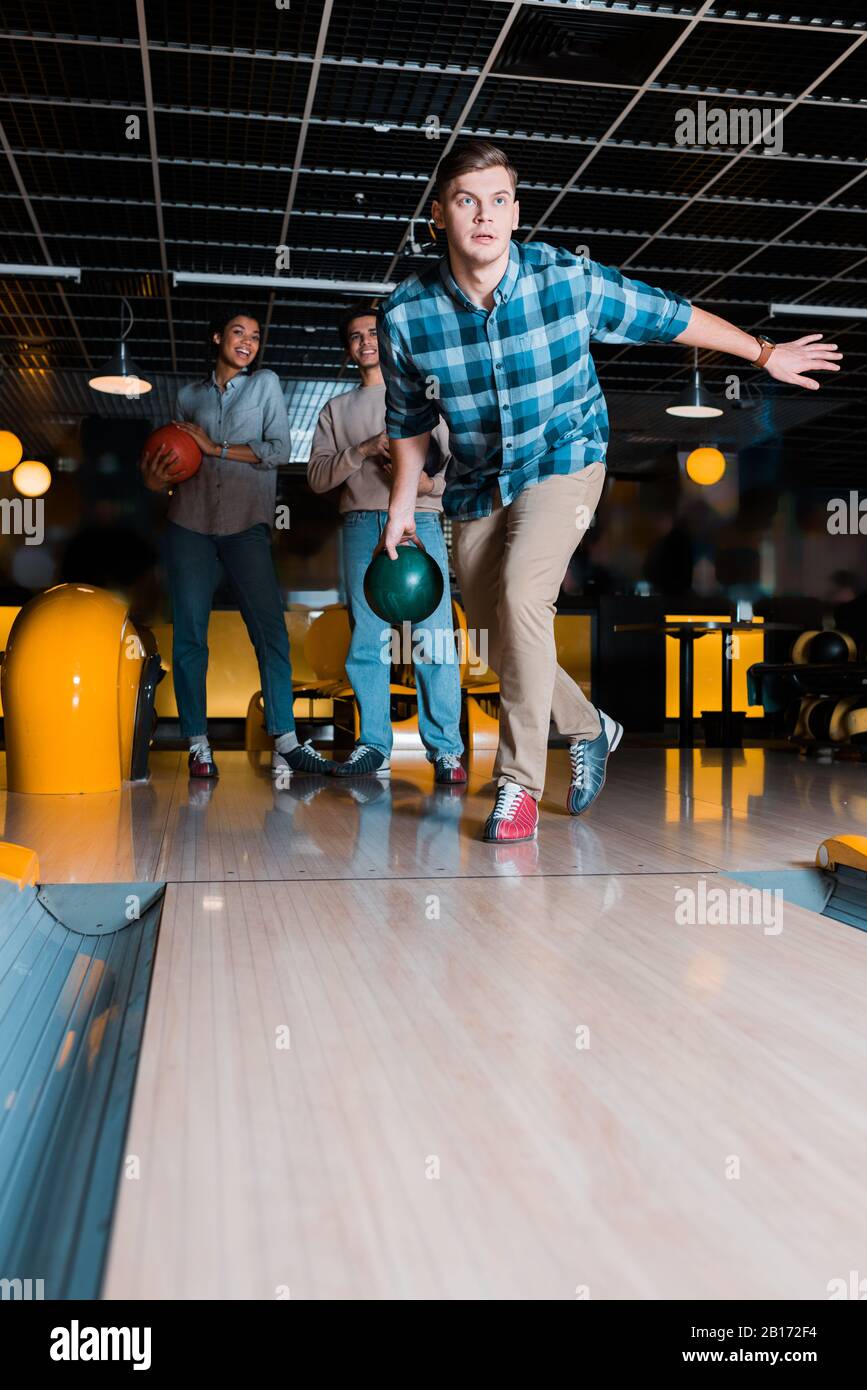 concentrated young man throwing bowling bowl on skittle alley near ...