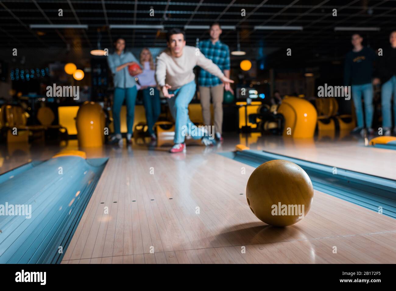selective focus of young man throwing bowling ball on skittle alley ...