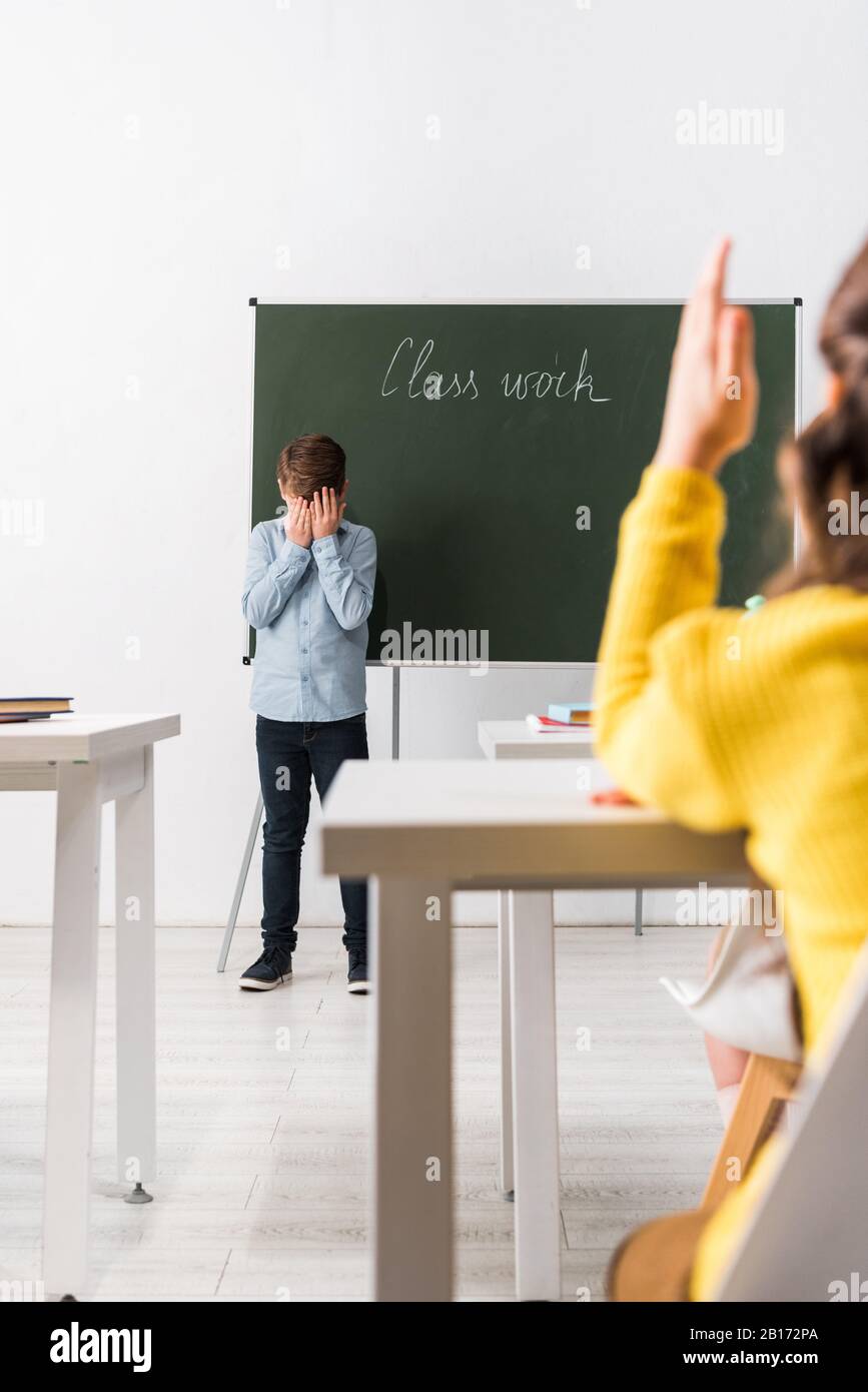 selective focus of upset schoolboy covering face while standing near ...